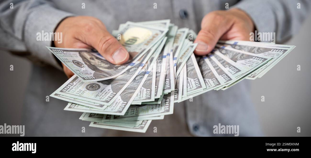 Hand holds roll of 100 dollar bills. Close up of someone hands holding ...