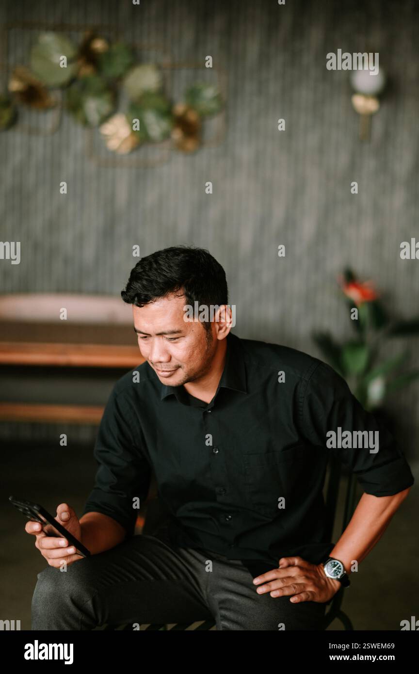 A contented man, immersed in his smartphone while seated indoors. The ...