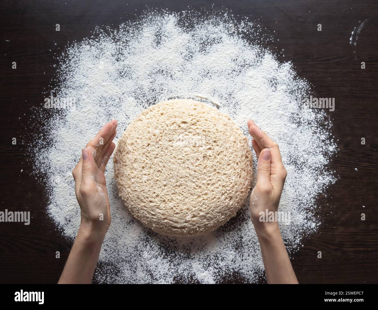 Baker's hand holds the raw yeast-free dough on a dark background. White ...