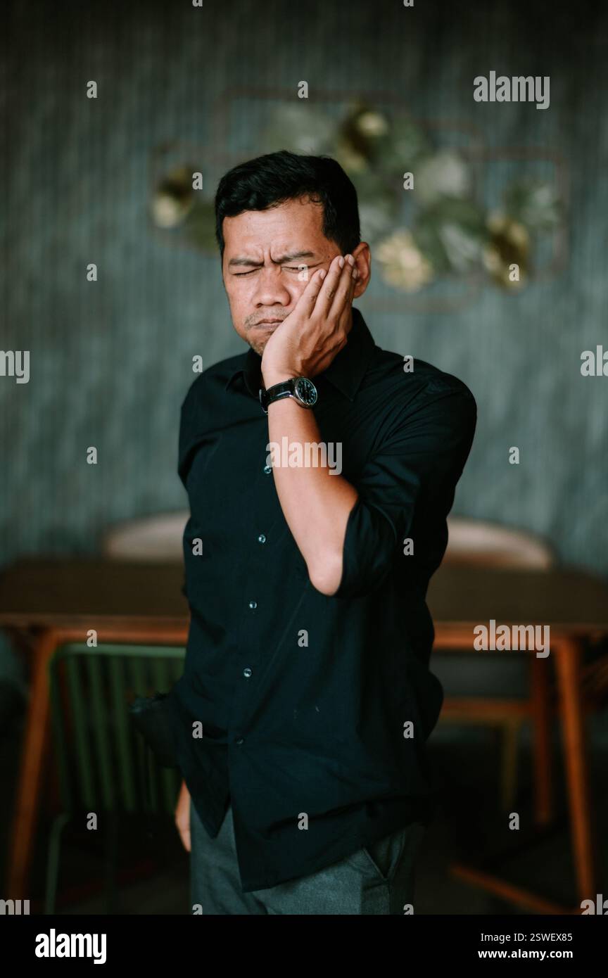 A man with a pained expression clutches his face, appearing to suffer ...