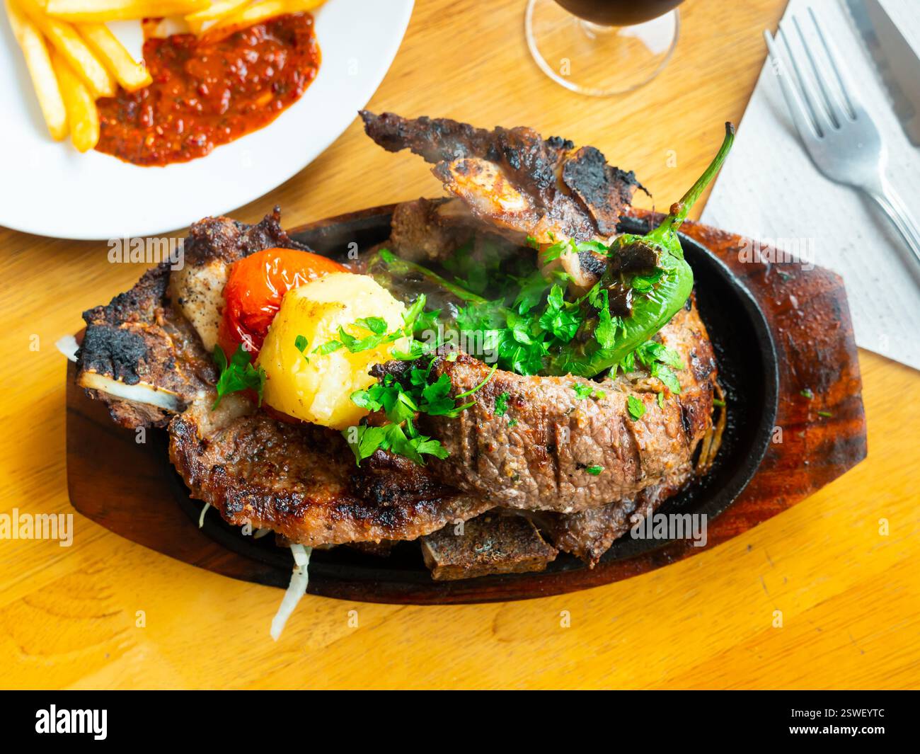 Hearty lunch of fried beef ribs in frying pan with vegetables and ...