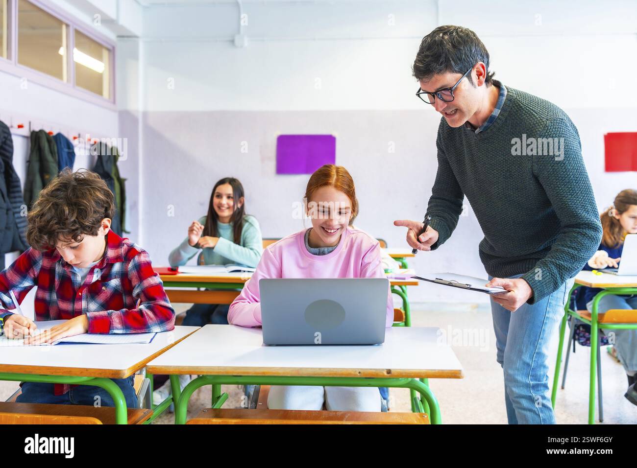 Teacher helping a smiling student using laptop computer in classroom ...