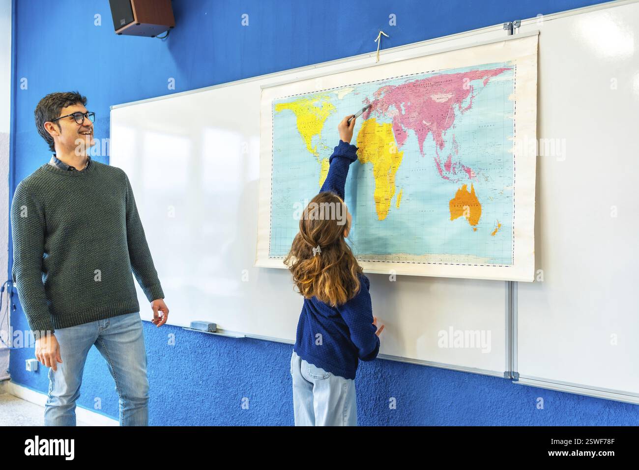 Smiling teacher watching elementary school student pointing at a world ...