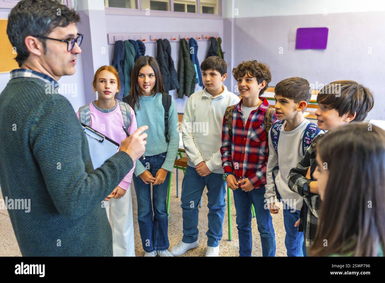 Male teacher holding clipboard explaining lesson to group of elementary ...
