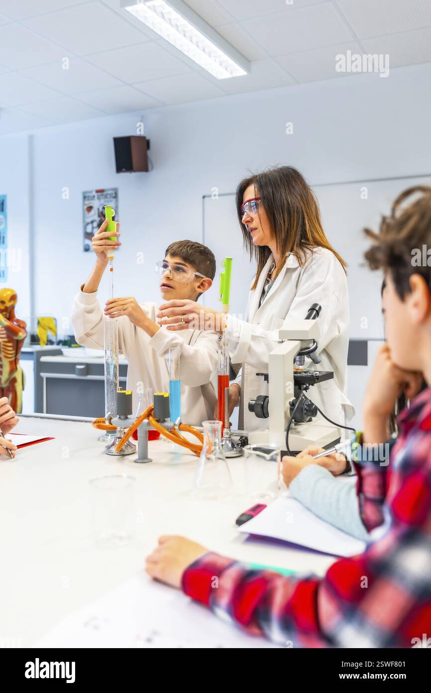 Students wearing safety glasses and lab coats conduct a chemistry ...