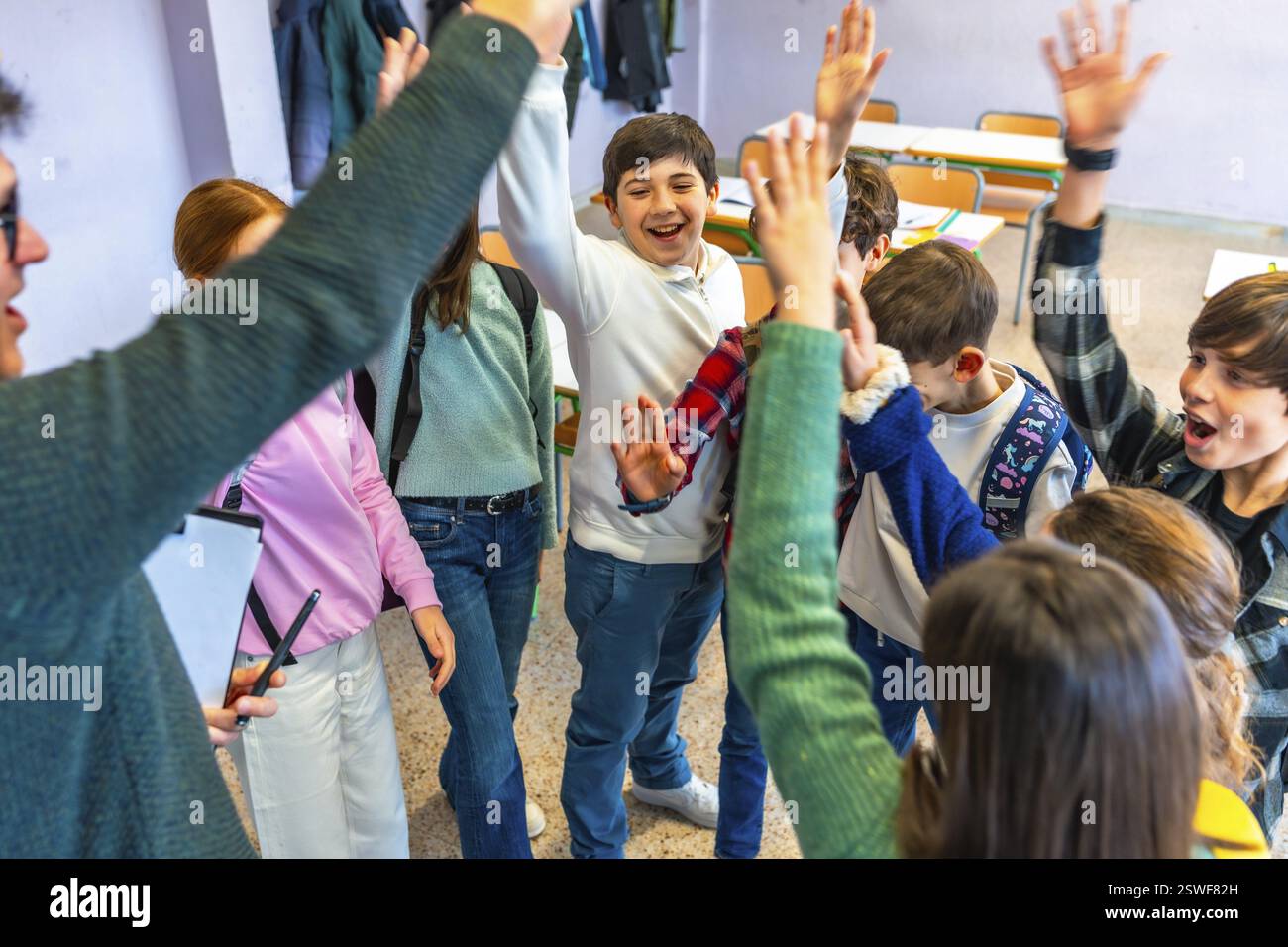 Group of cheerful elementary school students and teacher raising hands ...