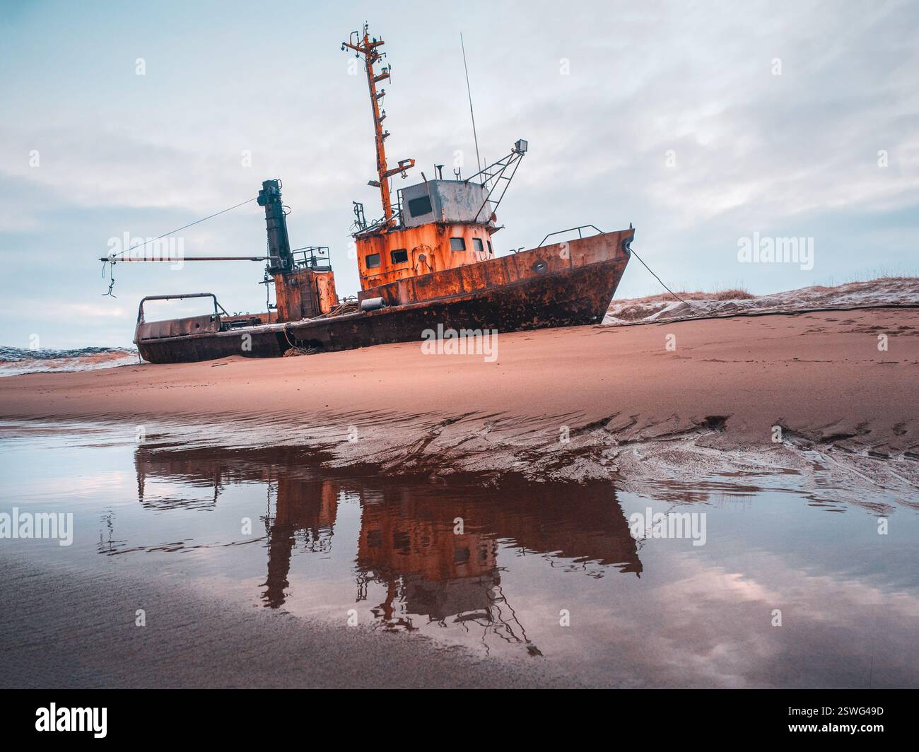An old rusty fishing boat washed up on a sandy beach in the Barents Sea ...