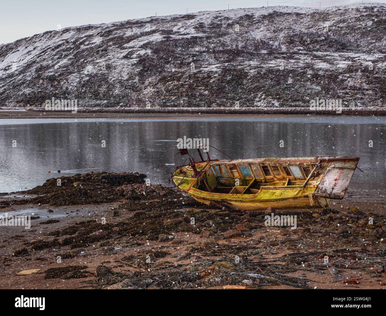 An old rusty fishing boat washed up on a sandy beach in the Barents Sea ...