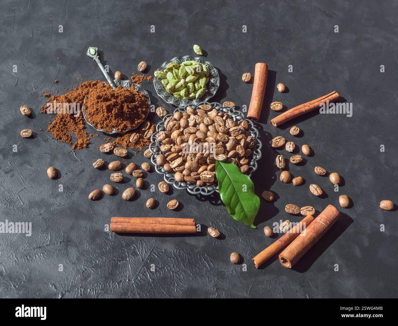 Coffee beans, ground powder, cinnamon and cardamom on black background ...