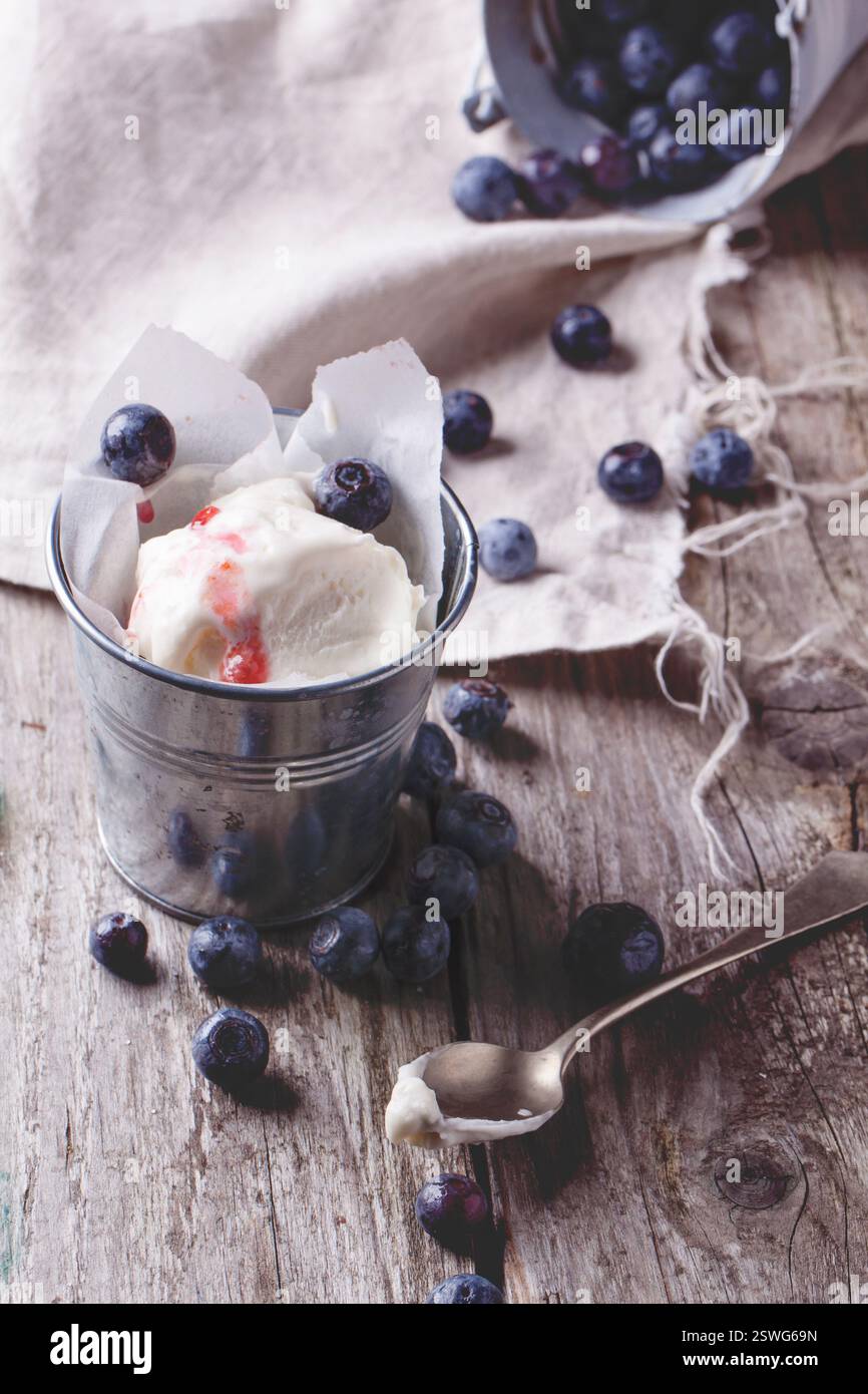 Ice cream, served in little metal pail with blueberries on old wooden ...
