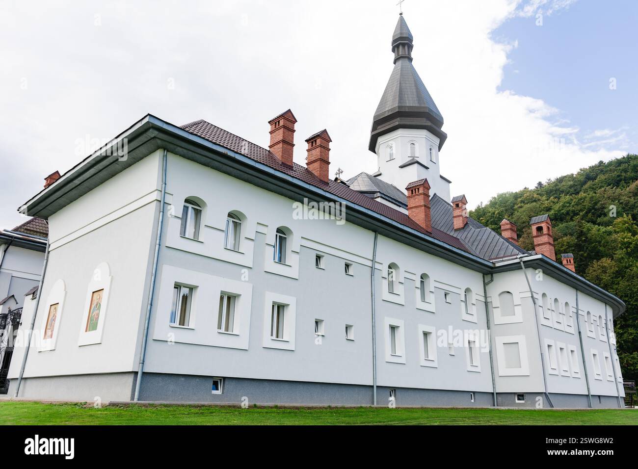 Modern monastery building with a tall tower and green hills in the ...