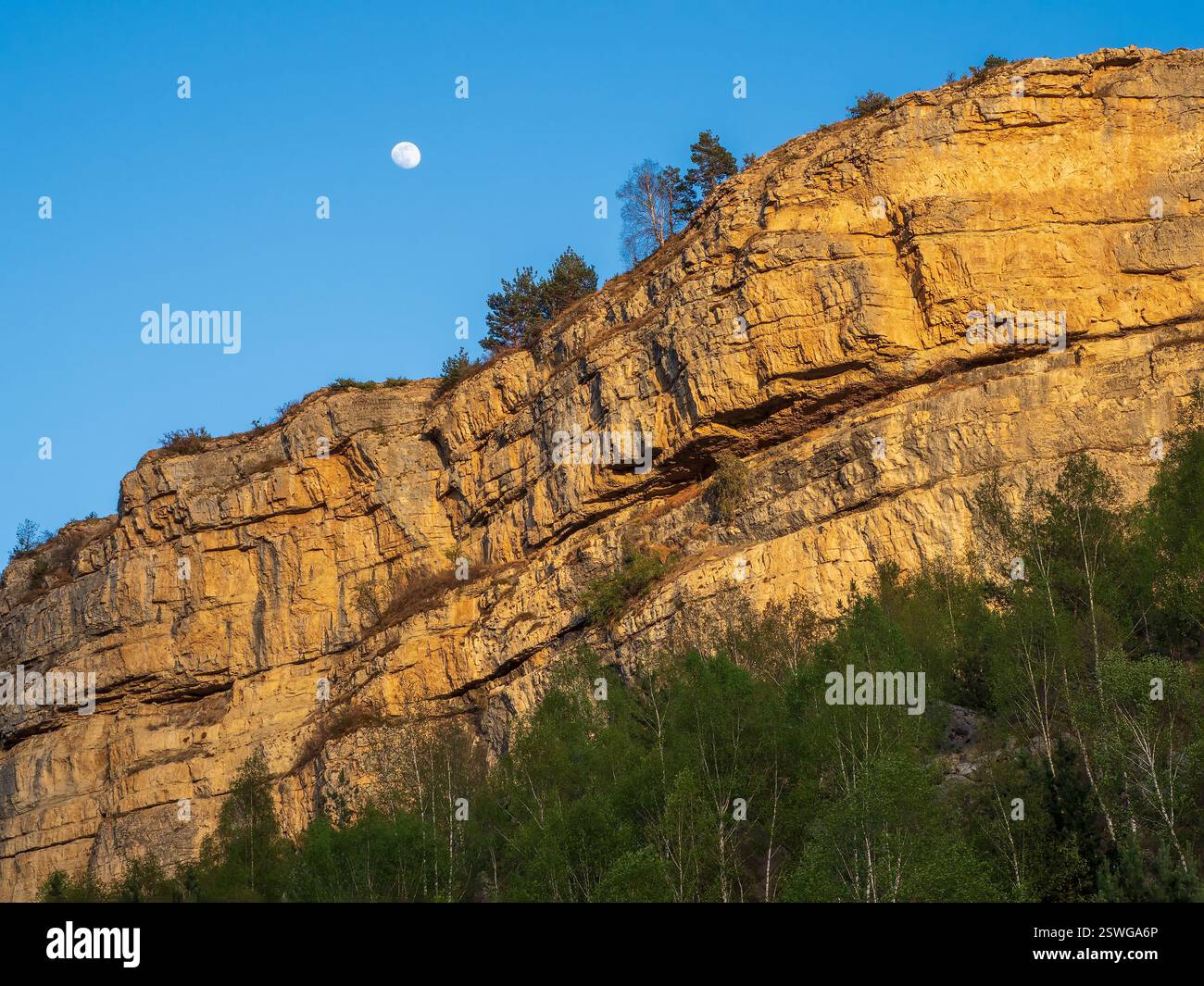 White moon is above the rock. Rock against the evening blue sky. High ...