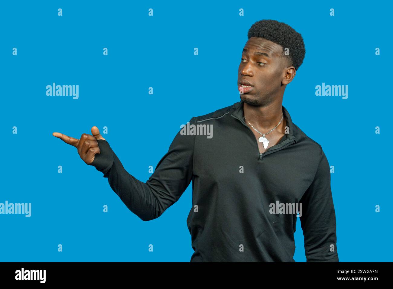 Studio shot of a young black man pointing and looking to the side ...