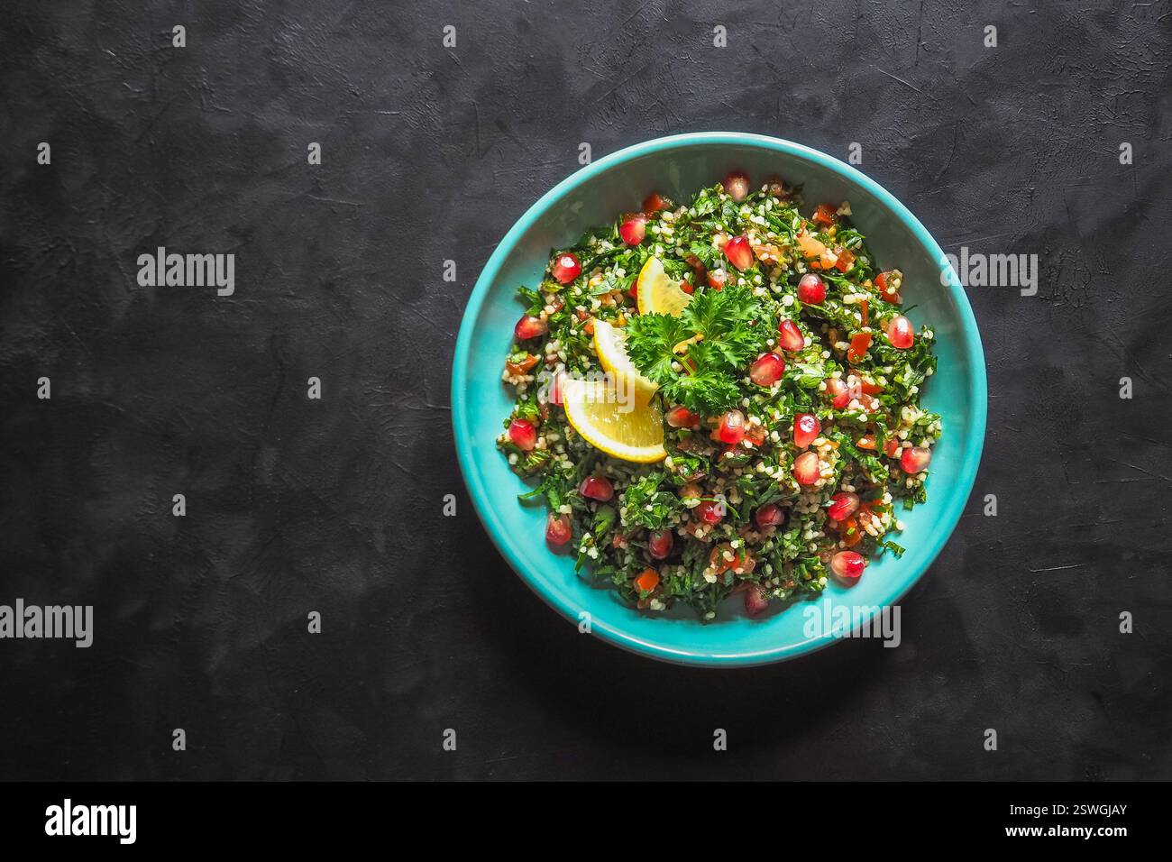 Tabbouleh salad with couscous in a bowl on the black table. Levantine ...