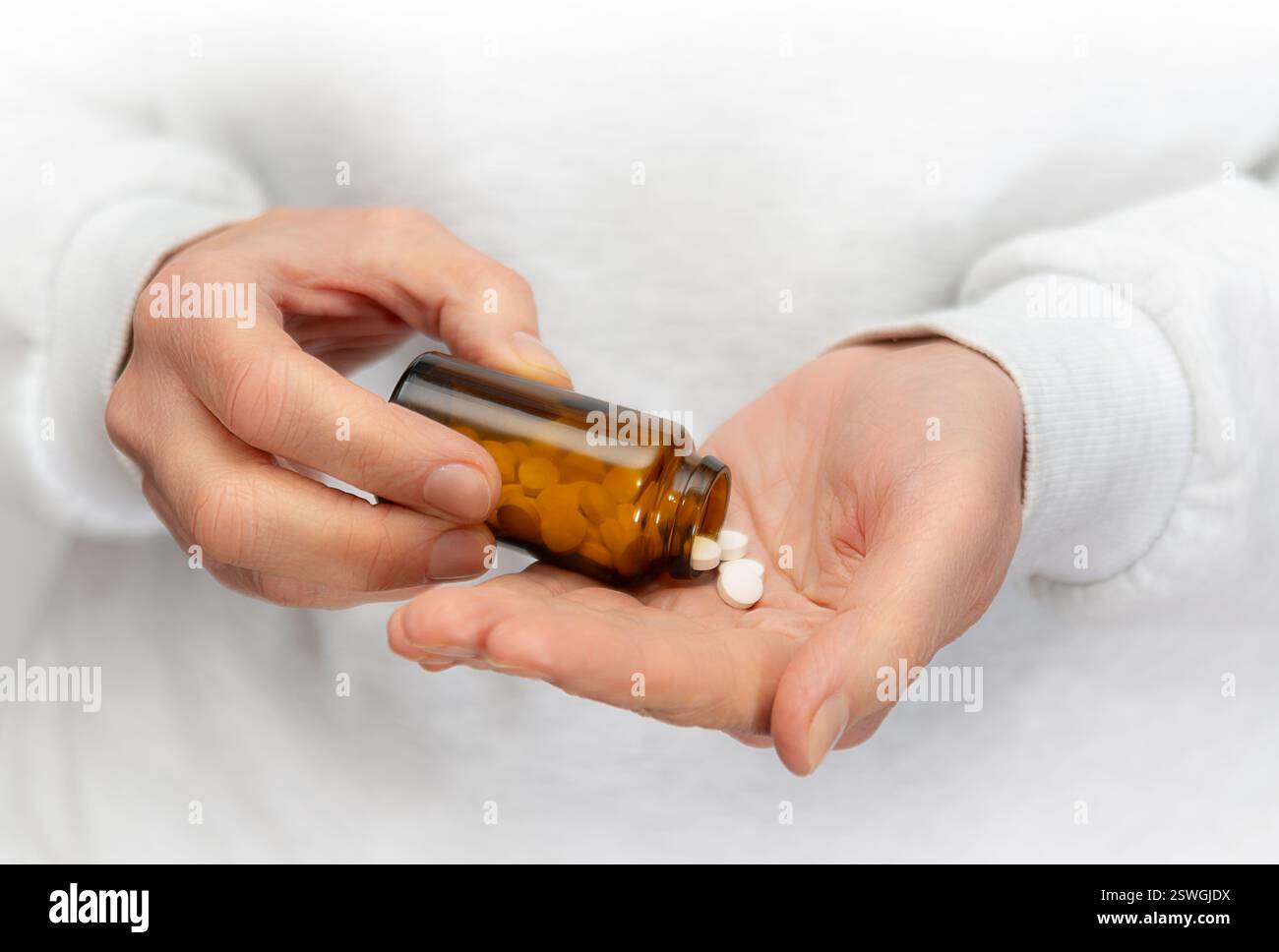 A person is carefully pouring white tablets from a brown pill bottle ...