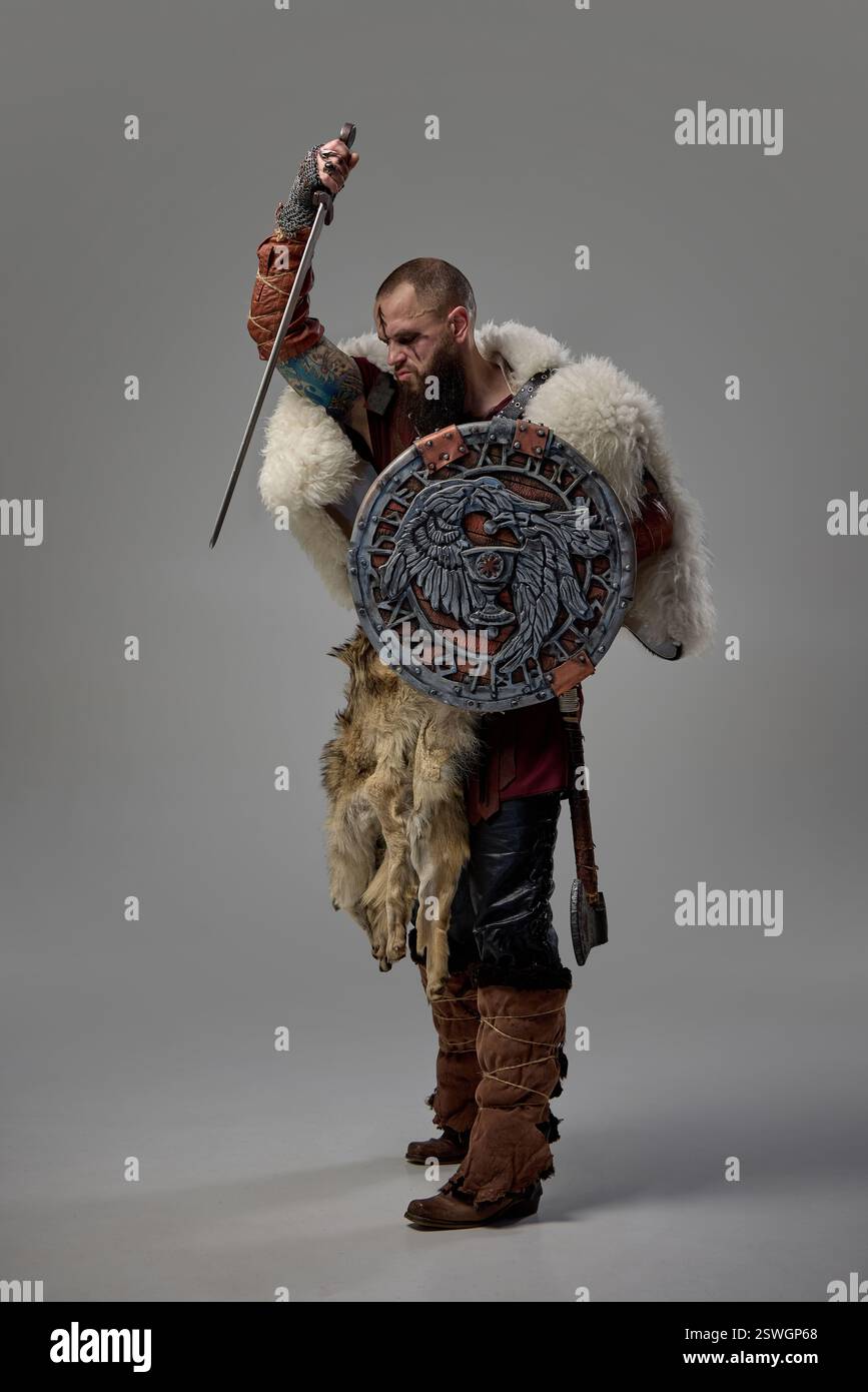 Portrait of man as medieval Viking warrior dressed in fur cloak and leather armor holding ...