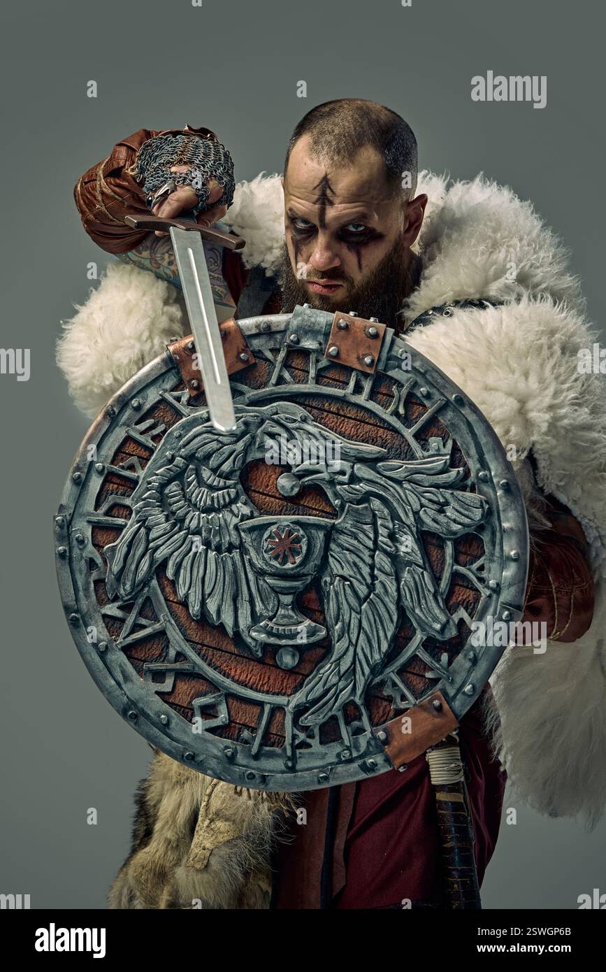 Man dressed as Viking warrior in medieval fur cloak, gripping sword ...