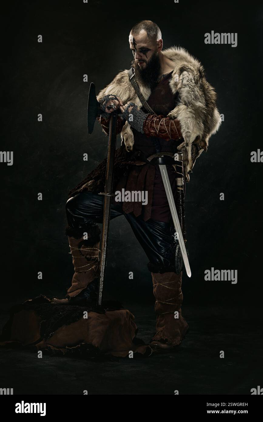 Viking warrior in rugged fur cloak, with axe and sword, standing in ...