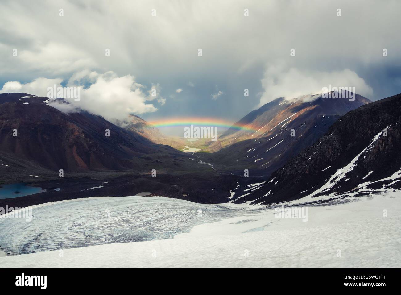 Rainbow over a mountain valley. Gloomy scenery with bright rainbow ...