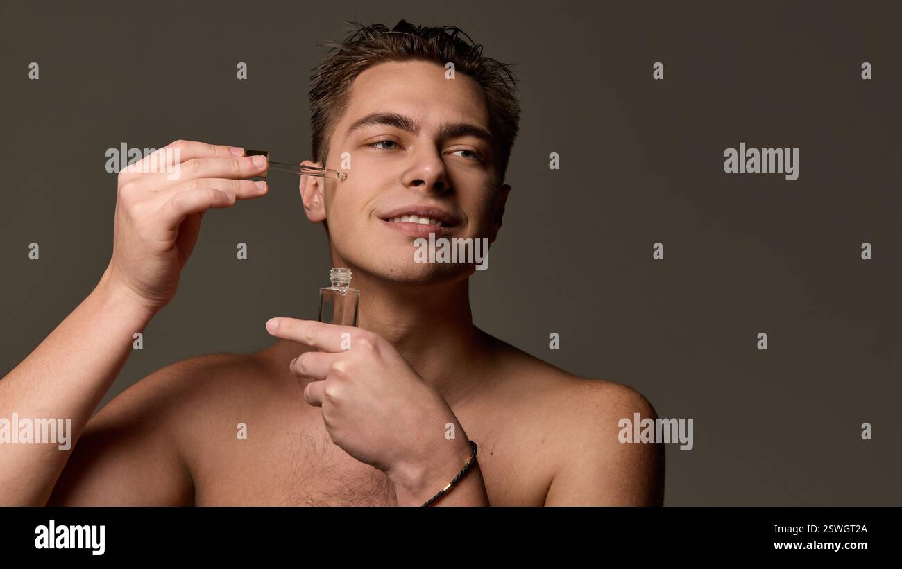 Man applying serum with dropper to cheek while holding glass bottle ...