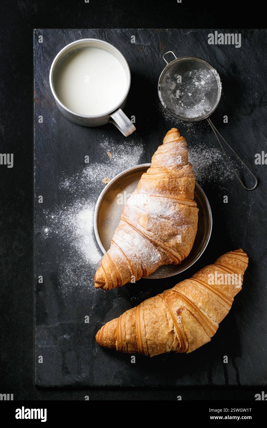 Two fresh baked croissants with sugar powder served with aluminum cup ...