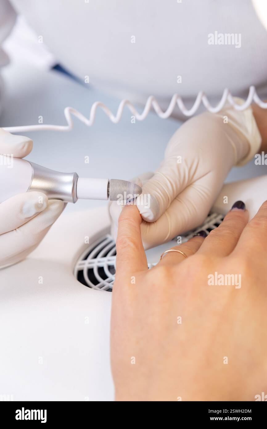 vertical photo of a manicurist who processes a client's manicure with ...