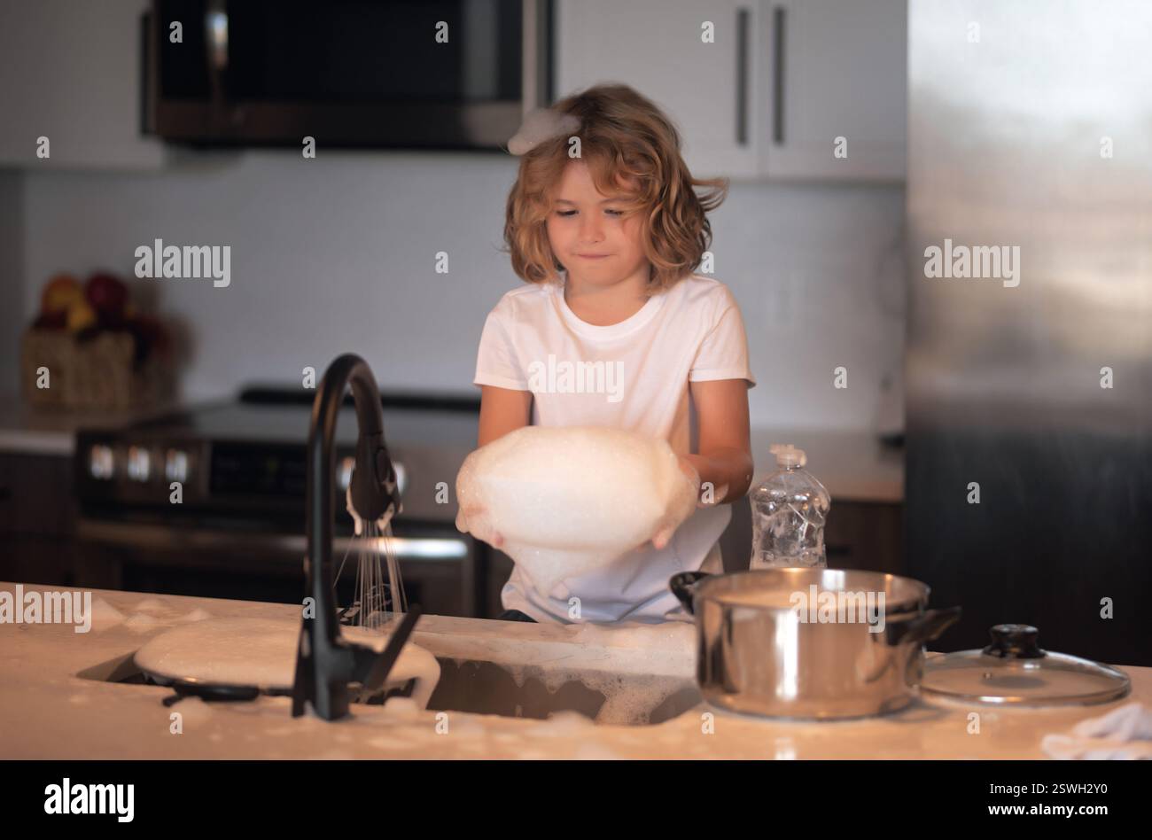 Kid boy washing dishes in the kitchen interior. Child helping his ...