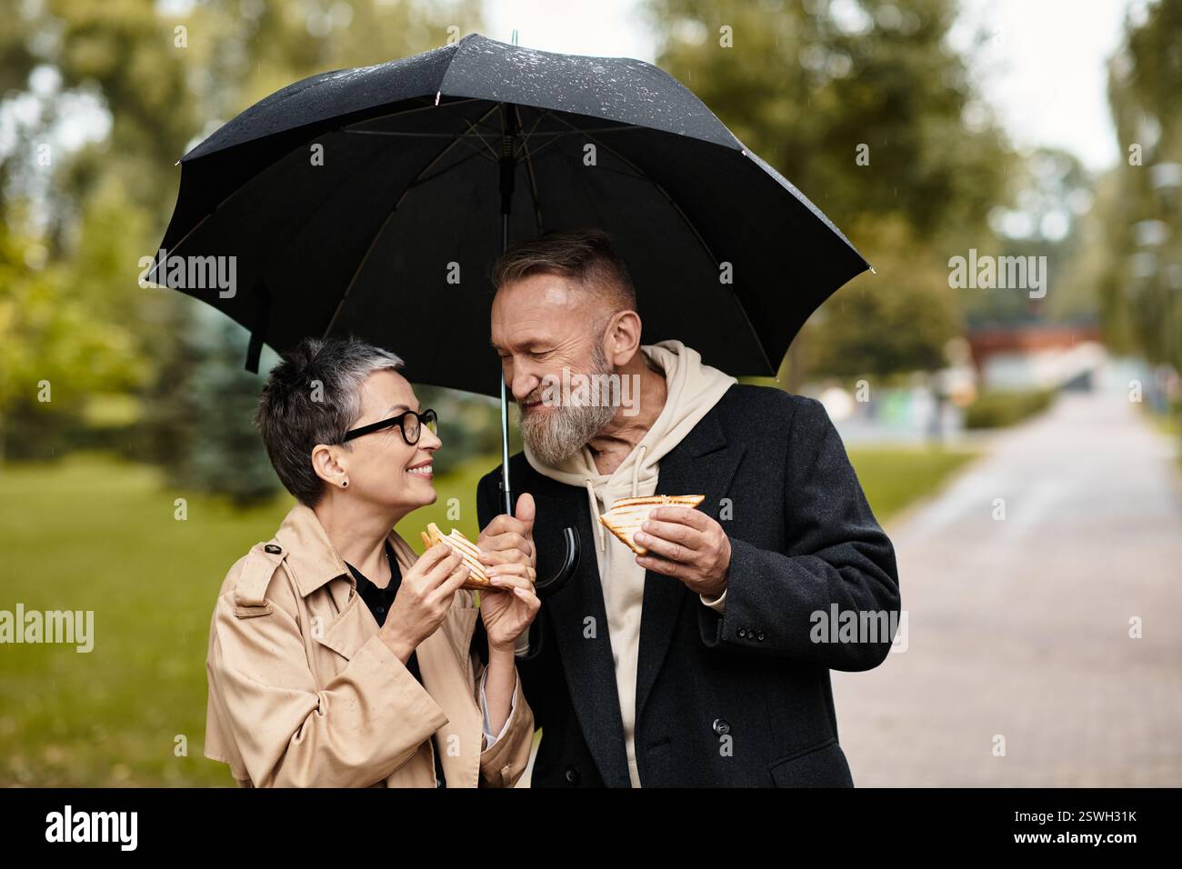 A loving couple enjoys sandwiches together while staying dry under a ...