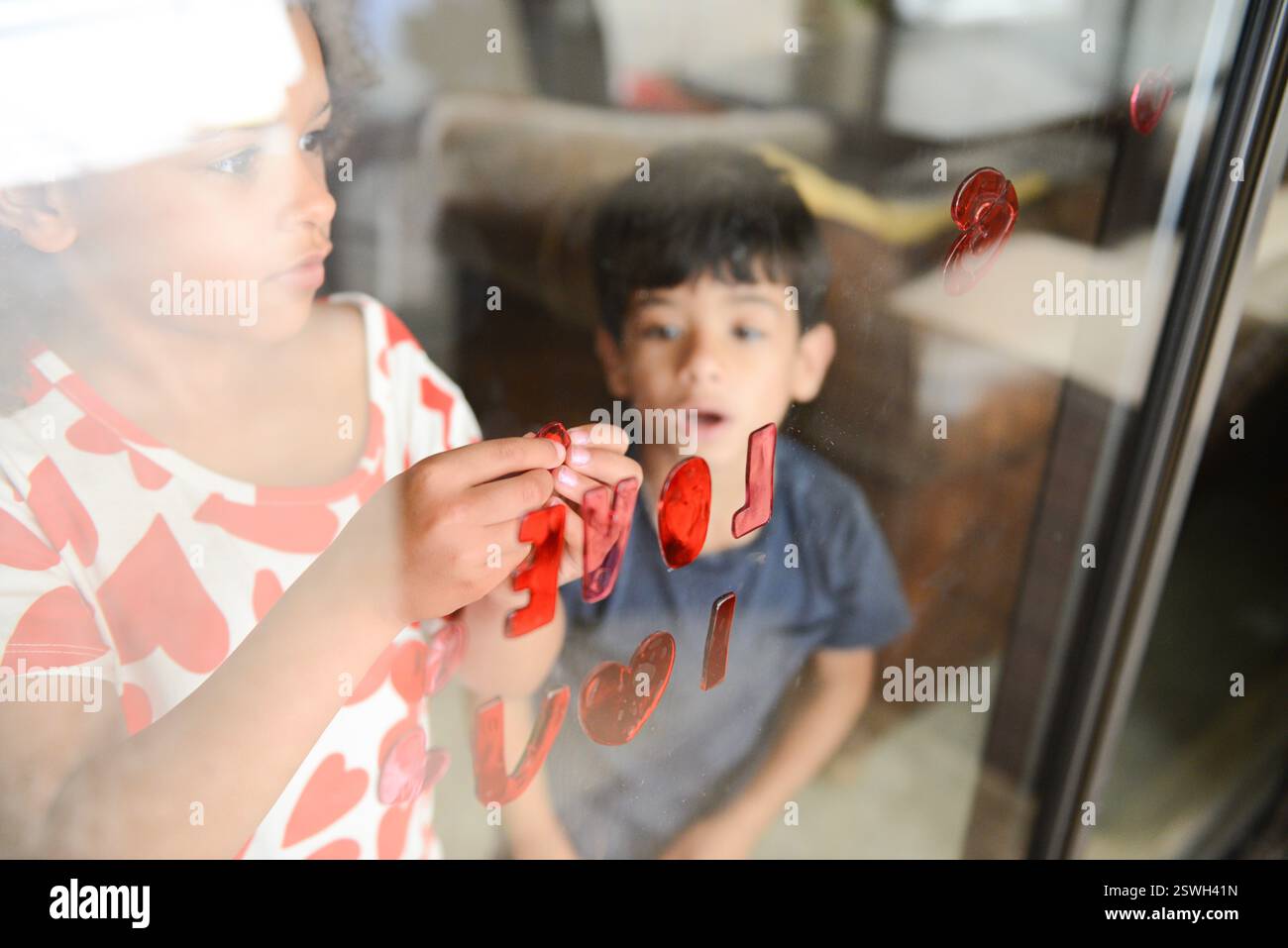 Two children decorate a window with red gel letters spelling "LO Stock ...