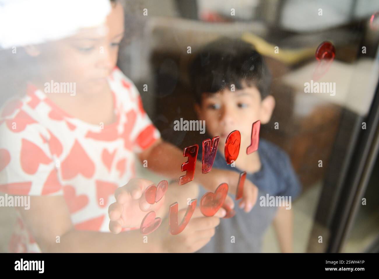 Two children decorating a window with red gel letters spelling Stock ...