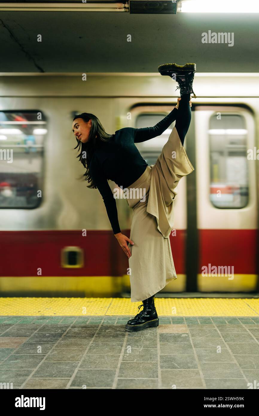 Woman balancing in dance pose on subway platform with train passing ...