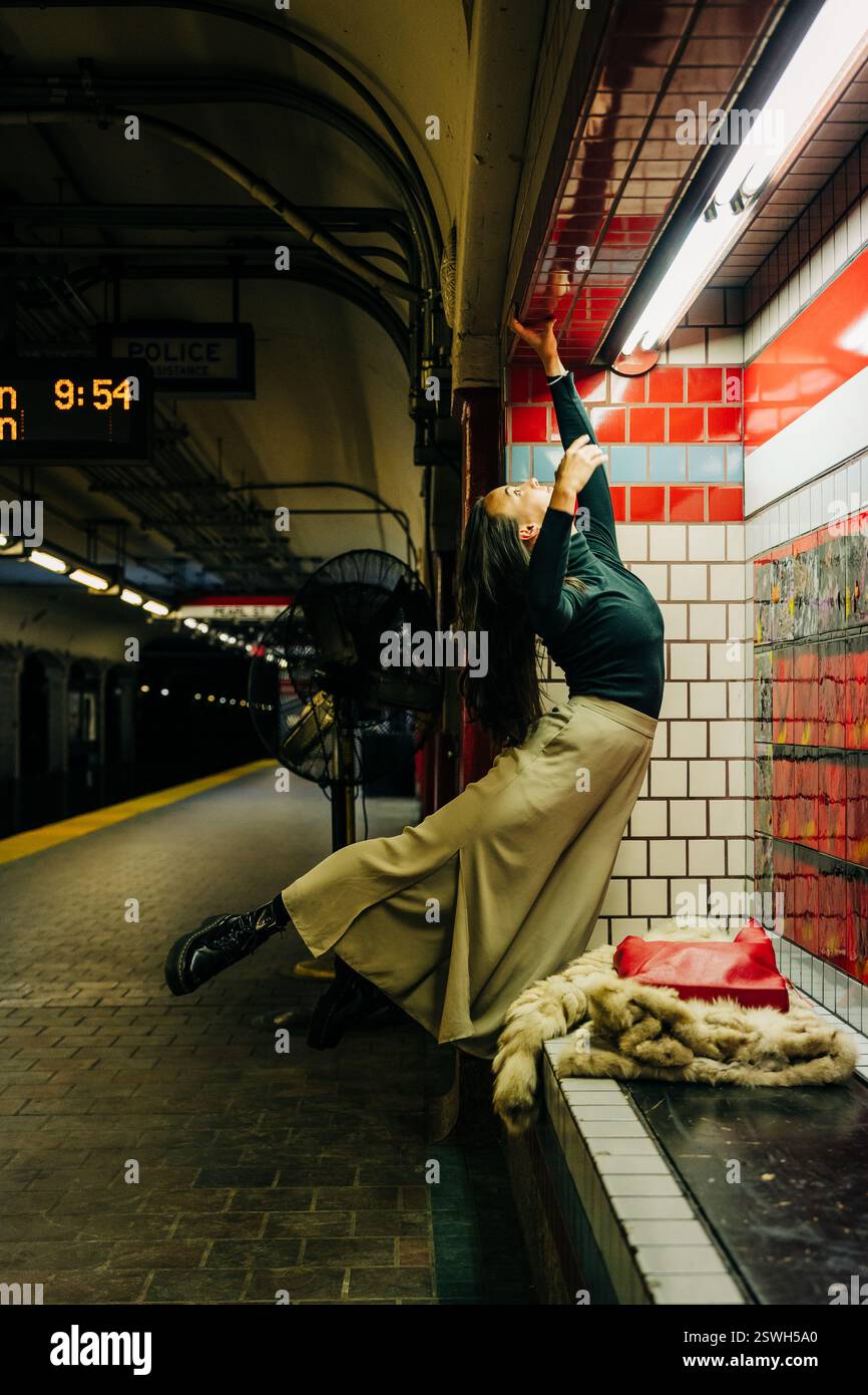 Woman dancing gracefully in subway station, reaching toward ceiling ...