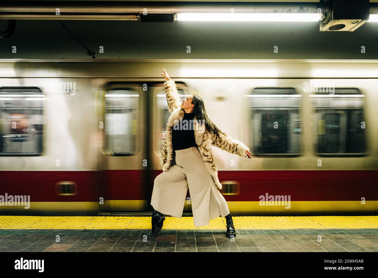 Woman in fur coat poses elegantly on subway platform with moving train ...