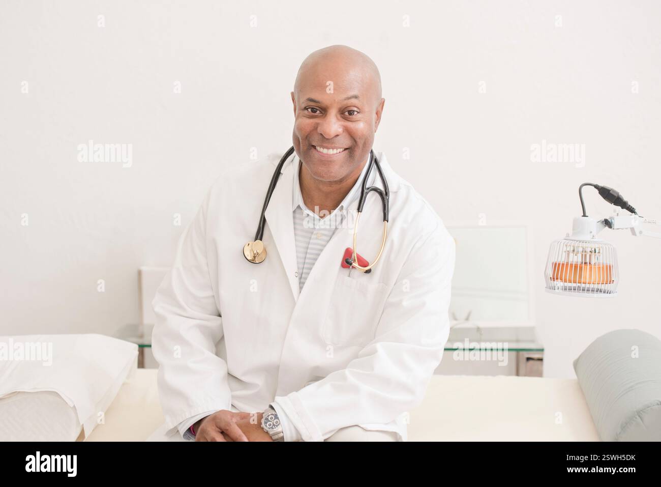 Smiling doctor in a white coat sitting in a medical examination room ...