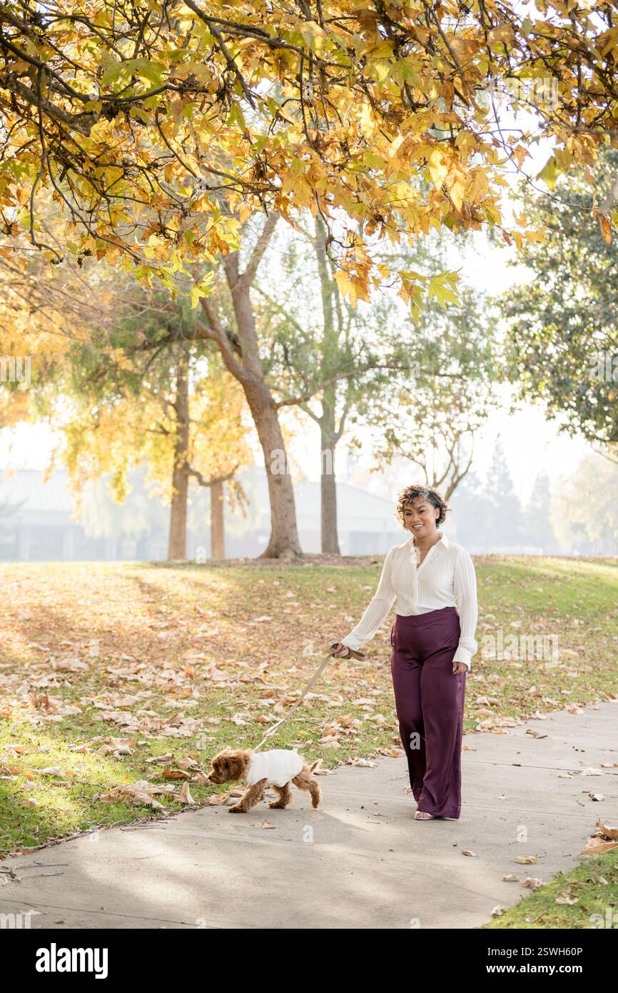 Woman walking her dog in a park with vibrant autumn foliage Stock Photo ...