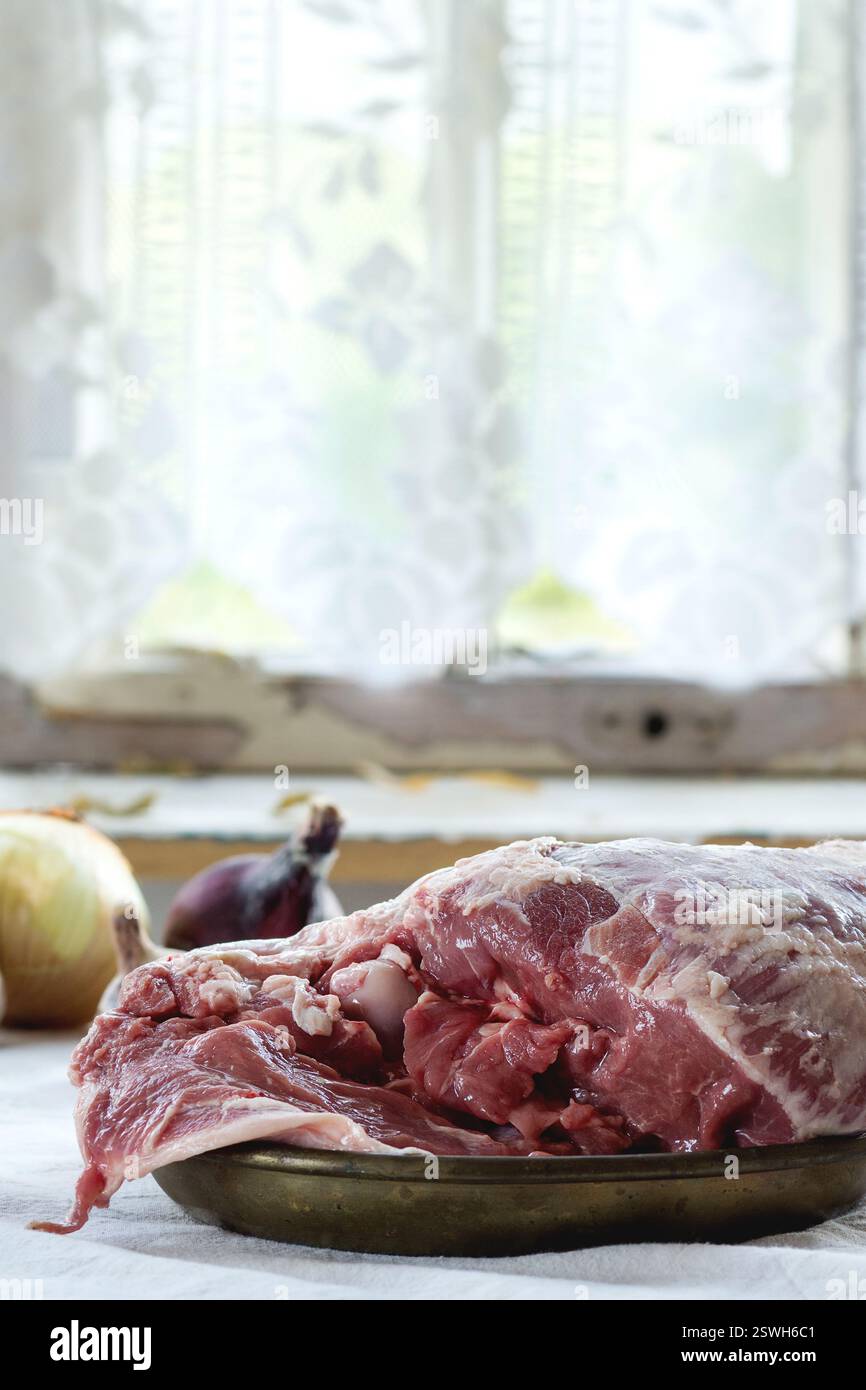 Raw loaf of lamb with onions over white kitchen table. With window as ...