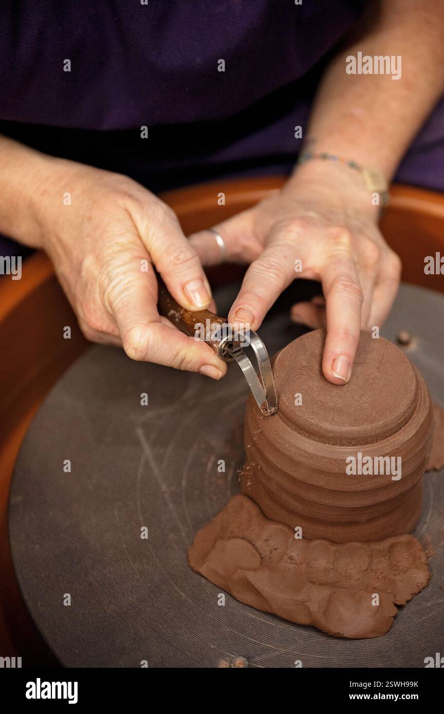 Artisan trimming a clay piece on a pottery wheel using a loop tool ...