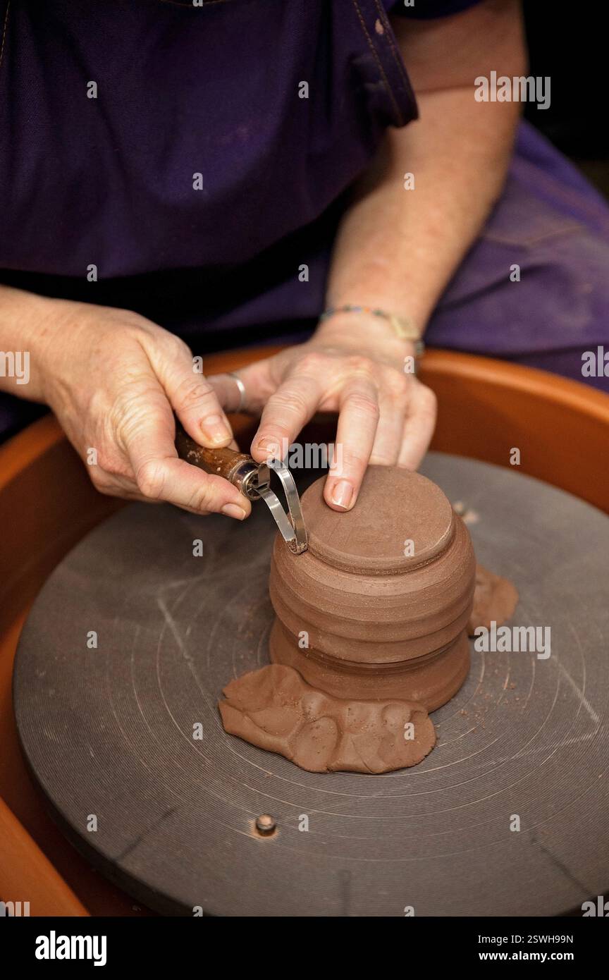 Artisan trimming a clay piece on a pottery wheel using a loop tool ...