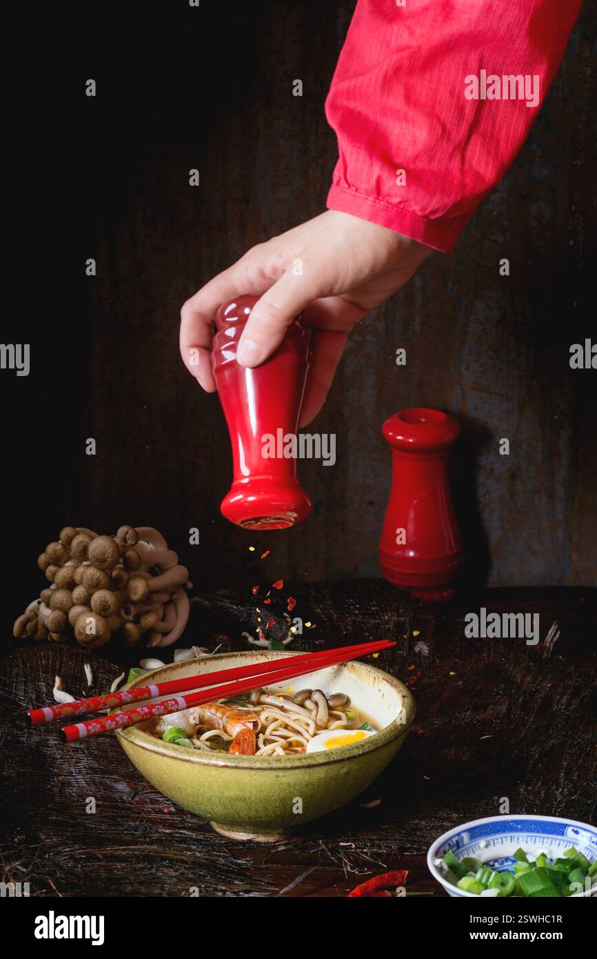 Female hand in red shirt sprinkle with pepper asian ramen soup with ...