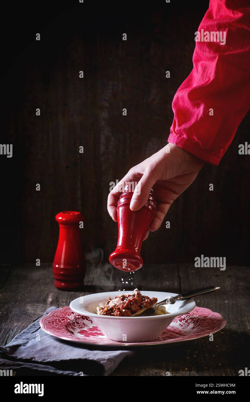 Female hand throws salt from red salt cellar into vintage english plate ...