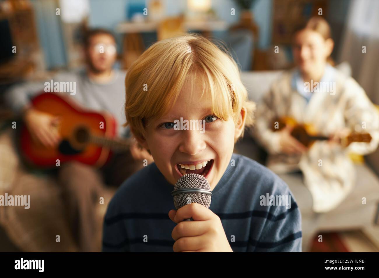 Blonde child joyfully singing into microphone while family members play ...