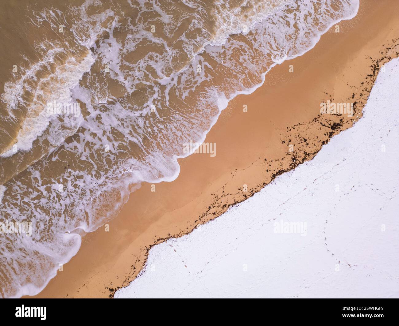 An overhead perspective of a winter shoreline where foamy ocean waves ...