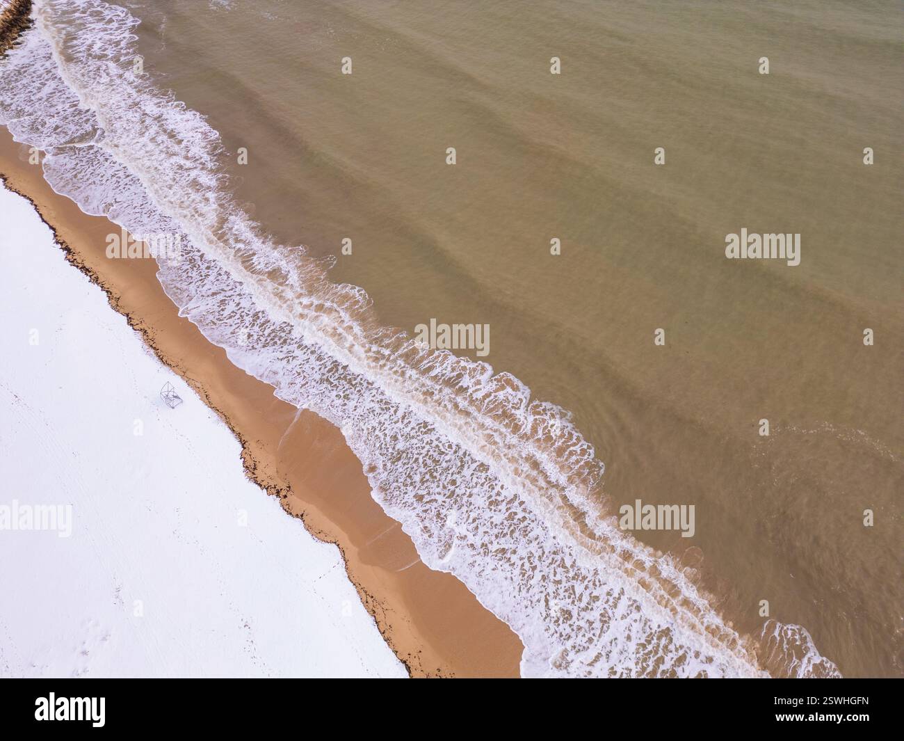 An overhead perspective of a winter shoreline where foamy ocean waves ...