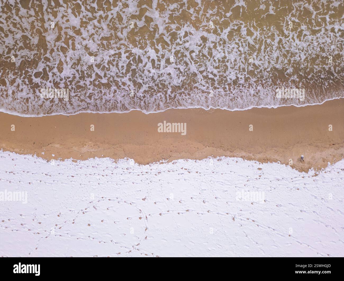 An overhead perspective of a winter shoreline where foamy ocean waves ...