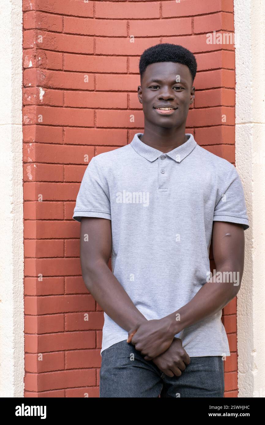 A man is standing upright in front of a solid brick wall, looking ...