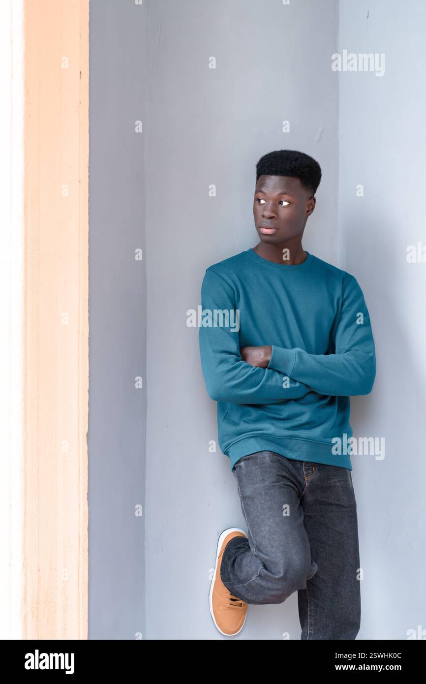 A man is leaning against a wall with his arms crossed in a confident ...