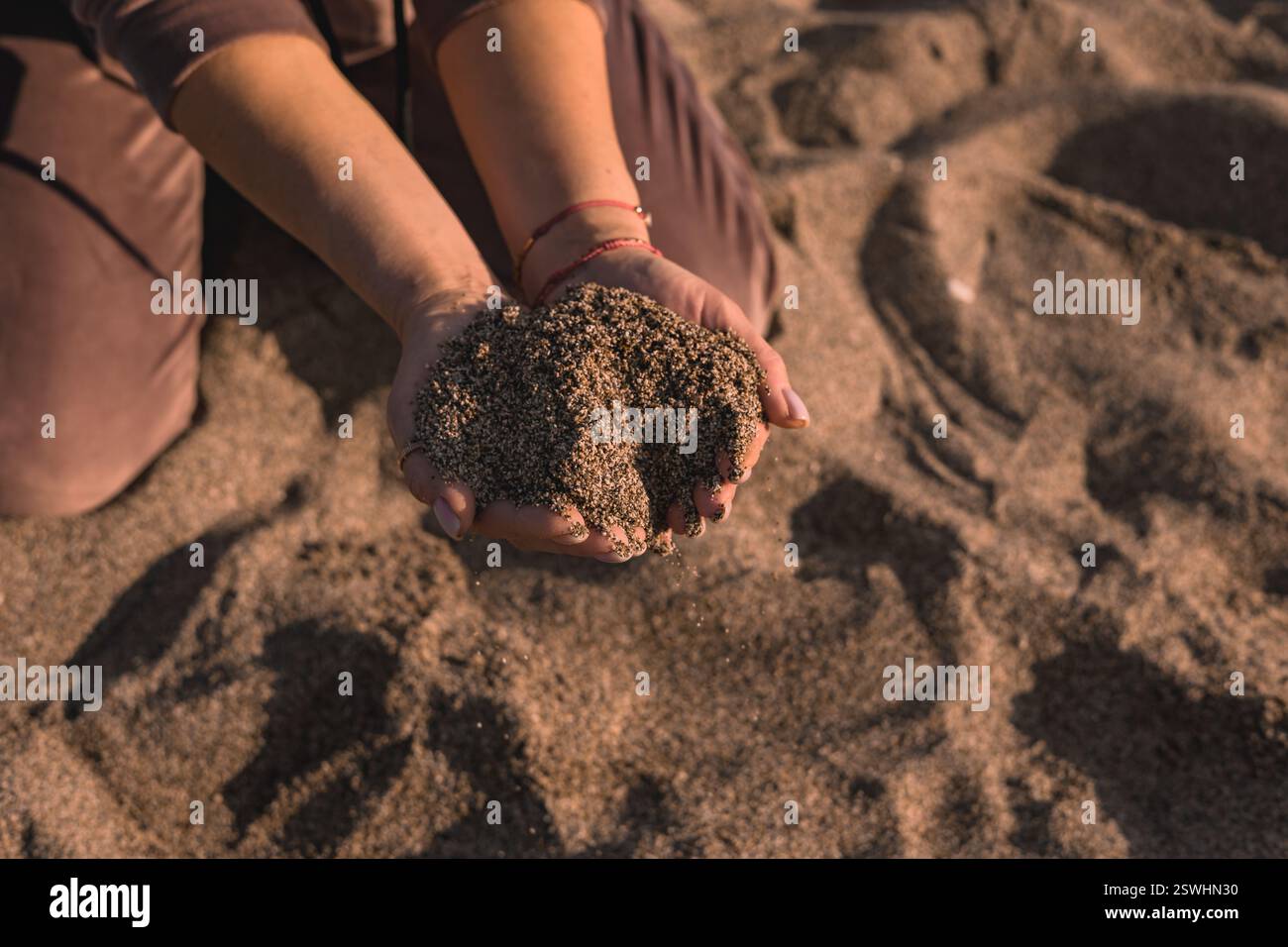 A person is gently cupping a handful of sand on a beach. The sunlight ...