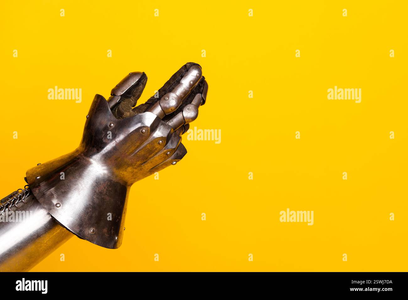 Metal knight's armored hands in prayer gesture against bright yellow ...