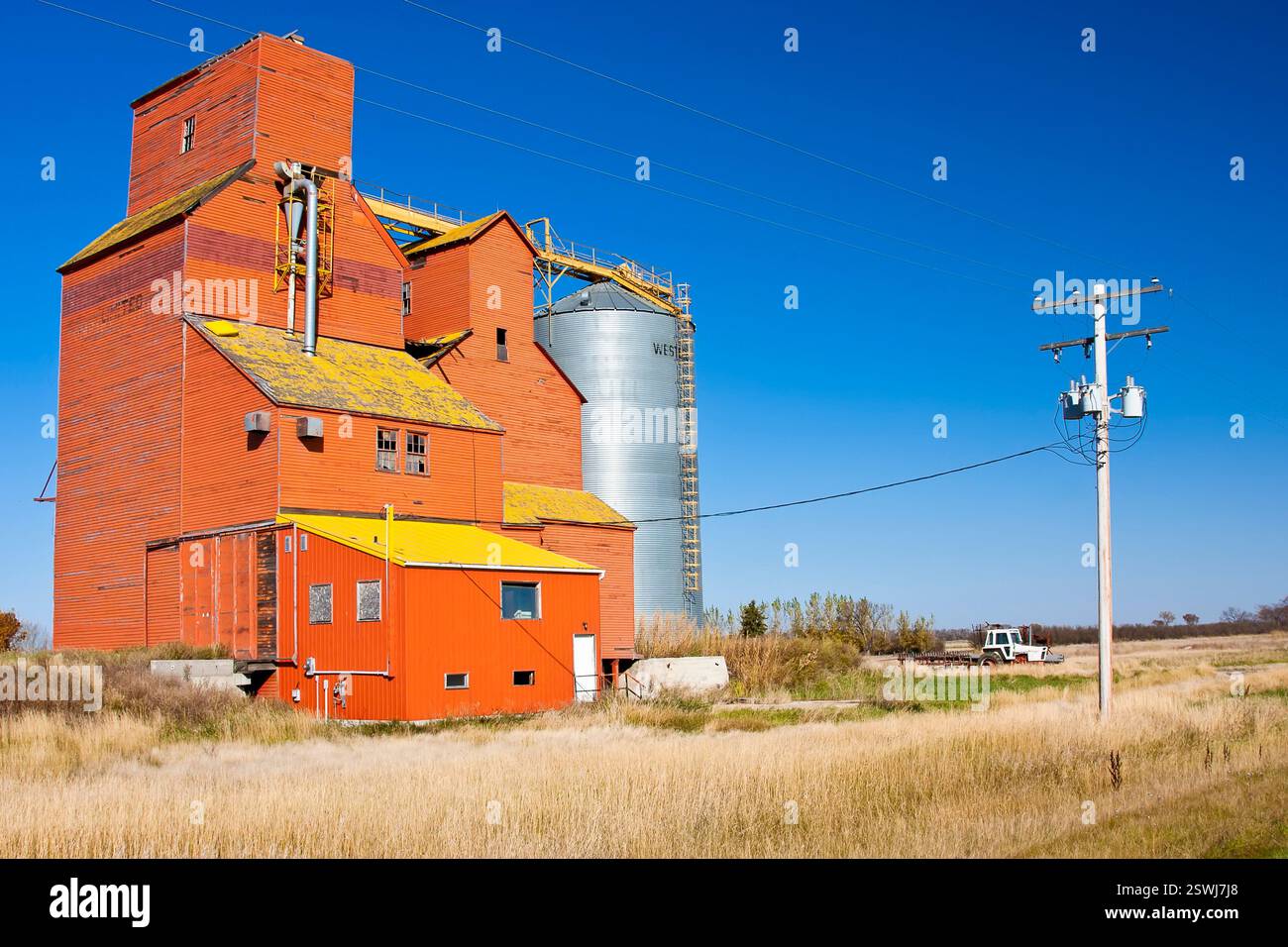 Red building with yellow trim sits in a field. The building is a grain ...