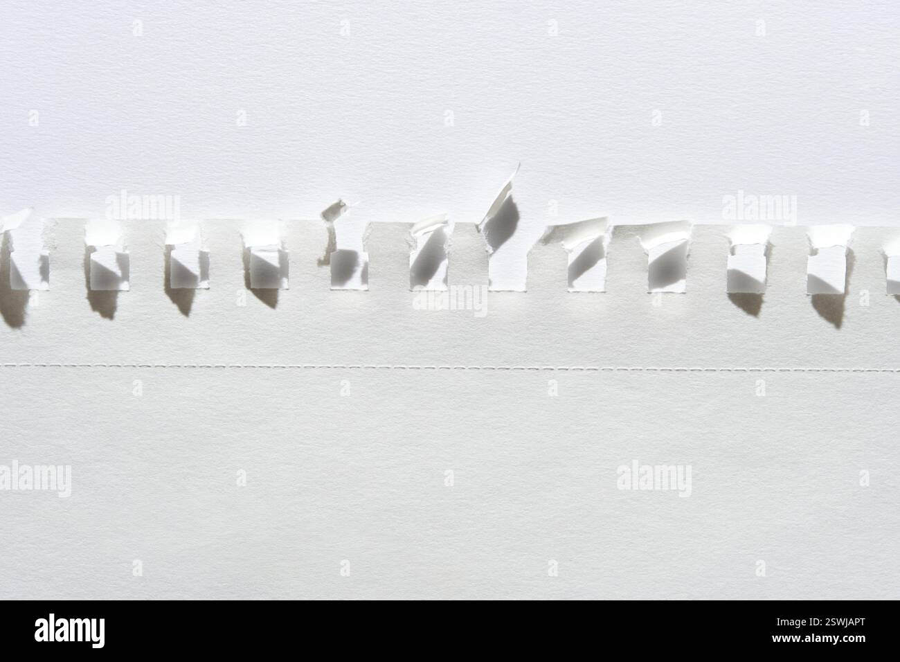 Close-up of torn white paper with perforated edge and folded tabs ...